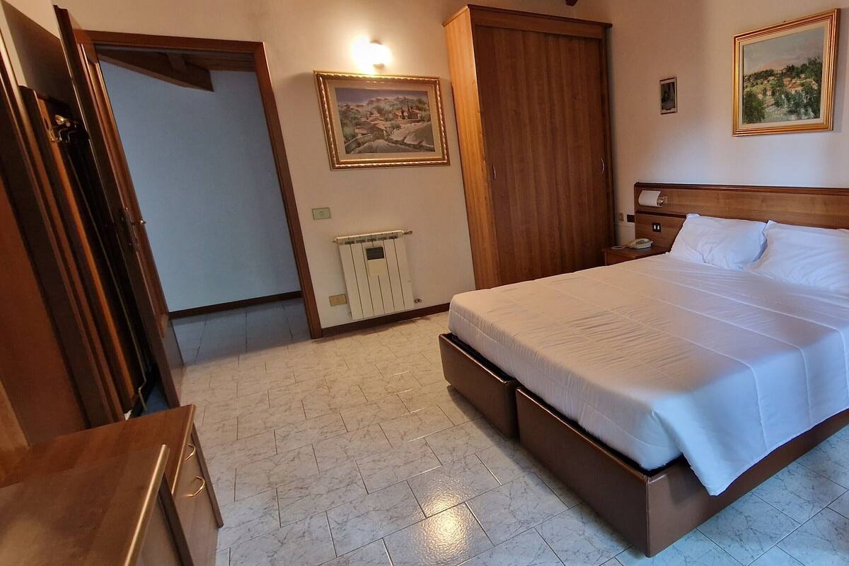 Quarto de hotel com uma cama grande, cabeceira de madeira, uma mesa de cabeceira, televisão e um guarda-roupa.