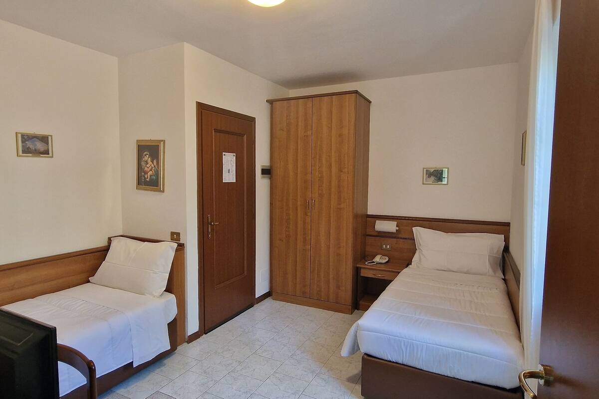 Quarto de hotel com duas camas de solteiro, um guarda-roupa de madeira, uma pequena mesa de cabeceira com um telefone e uma porta com um aviso.
