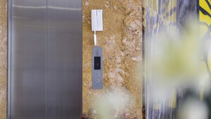 Um elevador com painel de comando digital e interfone fixado na parede.