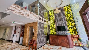 Um hall de entrada com piso de mármore, um balcão de recepção, um candelabro e uma parede com padrão floral amarelo.
