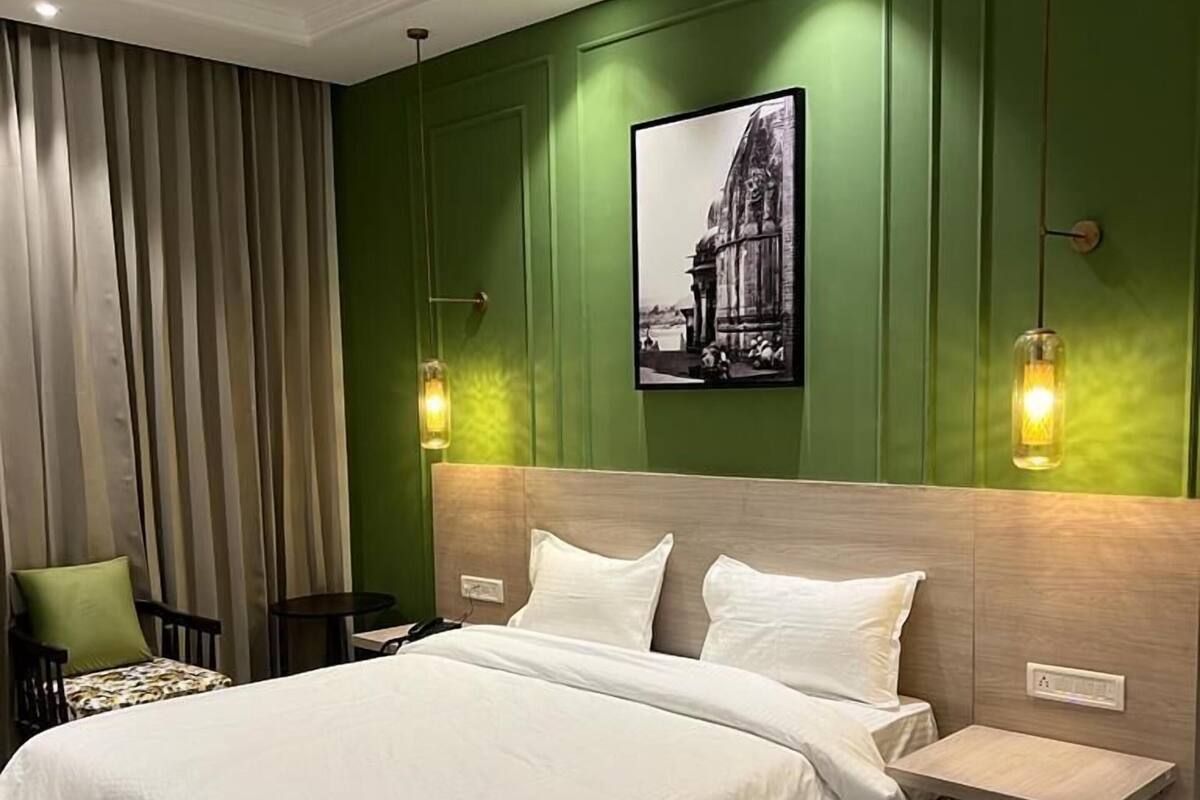 Quarto de hotel moderno com uma cama grande, paredes verdes, ventoinha no teto e um quadro emoldurado na parede.
