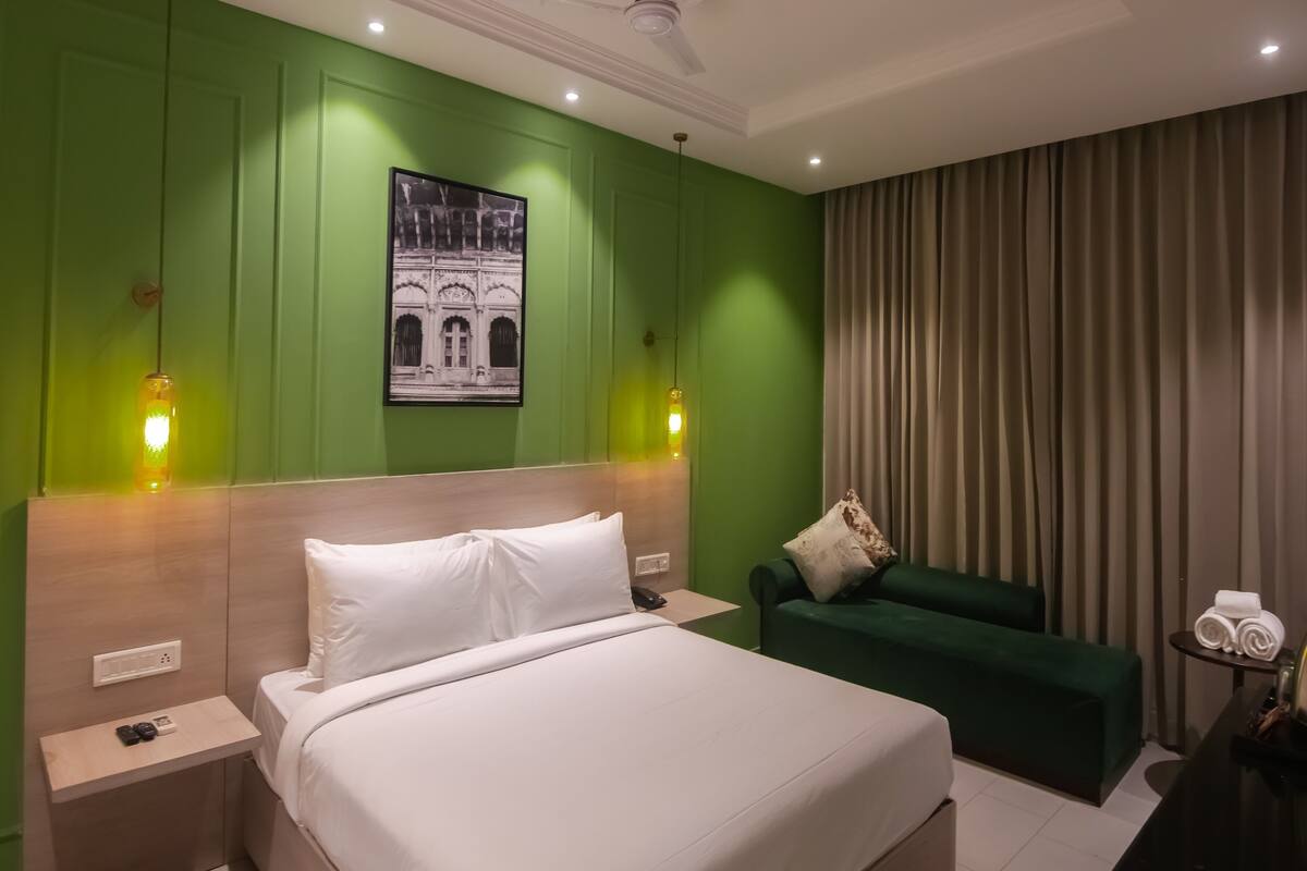 Quarto de hotel com uma cama, um sofá verde, um ventilador de teto e um quadro na parede.