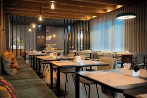 Restaurante moderno com vigas de madeira no teto, iluminação pendente e diversos assentos, incluindo mesas e um sofá.