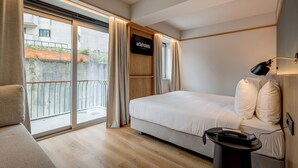 Quarto de hotel moderno com uma cama grande, uma mesinha de cabeceira com telefone e uma TV fixada na parede.