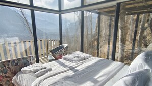 Quarto com uma grande janela com vista para uma paisagem montanhosa.