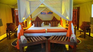 Quarto com cama sob dossel, duas mesas de madeira e almofadas estampadas.