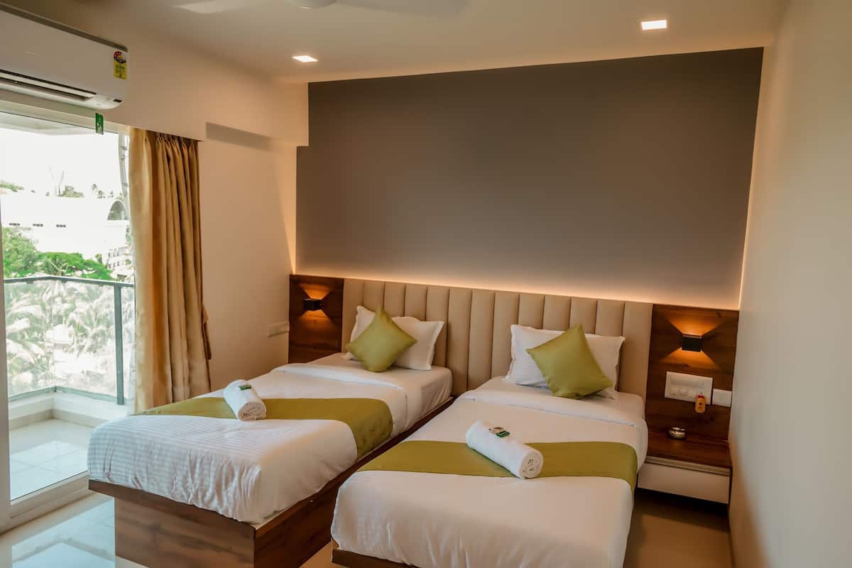 Quarto de hotel com duas camas, paredes bege e vista para o verde lá fora.