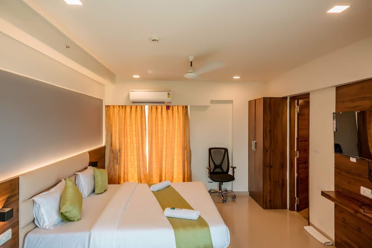 Quarto de hotel com cama, escrivaninha, cadeira, ar condicionado e armário.