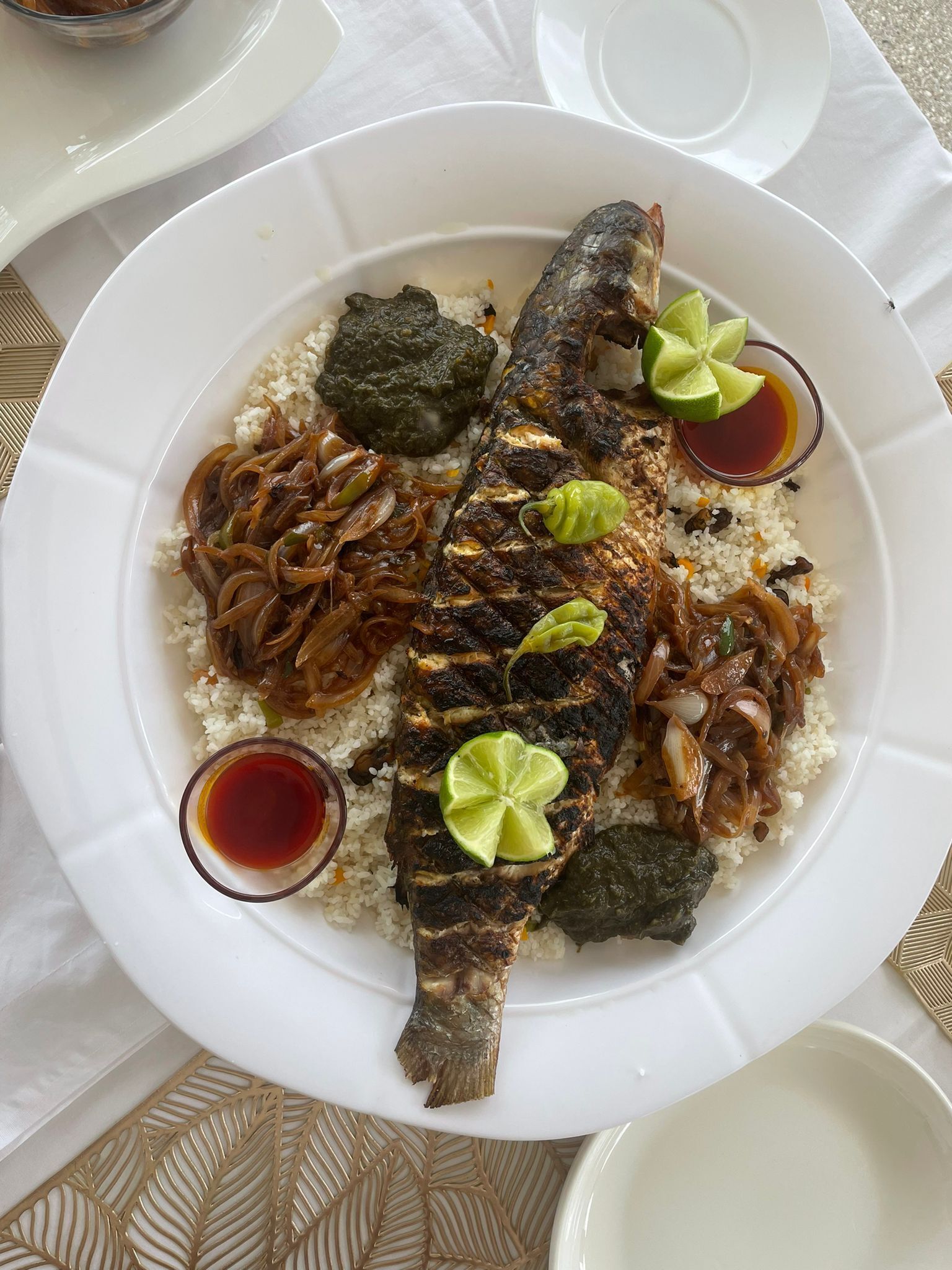 Prato de peixe grelhado com arroz, cebola e molho verde, servido em um prato branco.