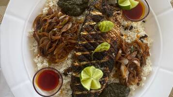Prato de peixe grelhado com arroz, cebola e molho verde, servido em um prato branco.