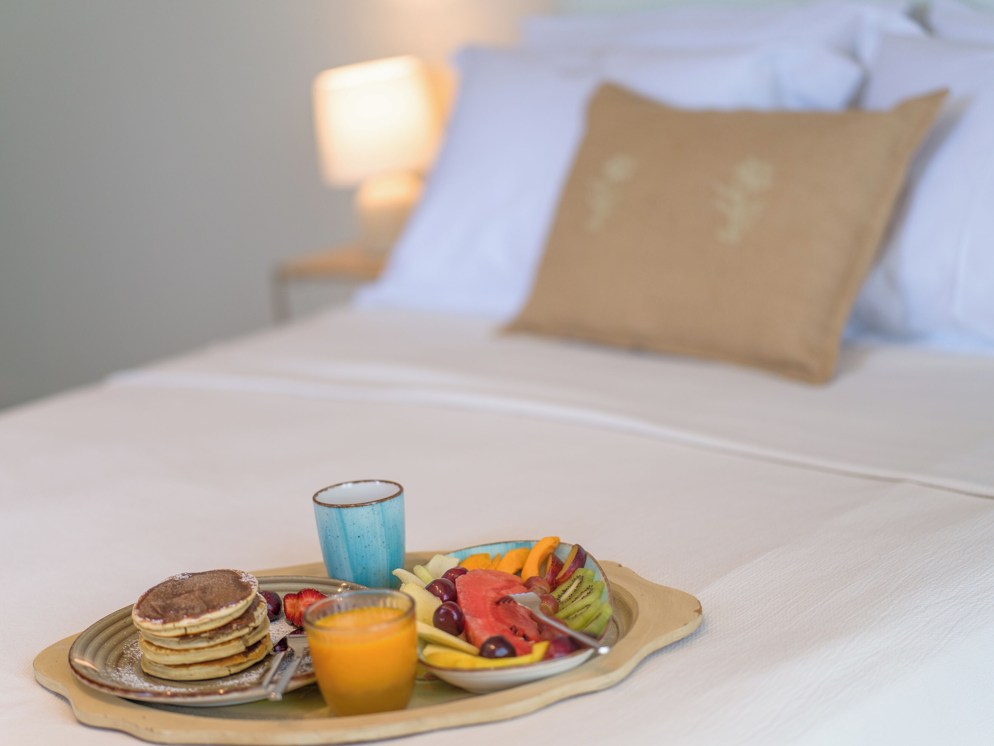 Bandeja de café da manhã com panquecas, frutas e suco de laranja sobre a cama.