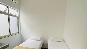 Quarto pequeno e limpo com duas camas de solteiro, uma janela e piso de madeira.