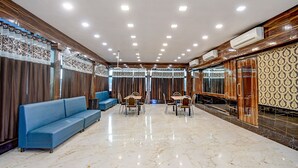 Um hall amplo com um sofá azul, uma área de refeições com mesas e cadeiras, e uma parede estampada.