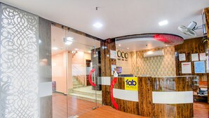 Uma área de recepção de hotel com balcão de madeira, divisórias de vidro e escada que leva a um andar superior.