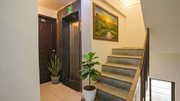 Um saguão de hotel com escadas, uma pintura e plantas em vasos.
