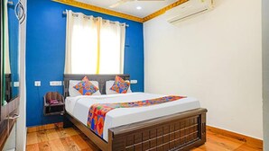 Quarto com cama, mesa de cabeceira, cômoda e janela com cortinas.