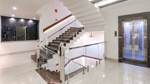 Interior moderno com escada em guarda-corpo de vidro, piso de mármore e elevador panorâmico.