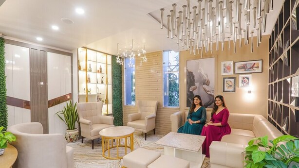Uma sala de estar moderna com um sofá, poltronas, uma mesa de centro e um lustre decorativo.
