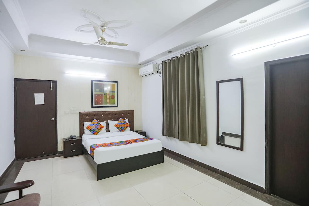 Quarto de hotel com cama, mesa de cabeceira, cadeira, ventoinha no teto, janela com cortinas e porta.