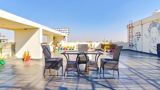 Terraço no telhado com mesa e cadeiras, plantas em vasos e um mural na parede.