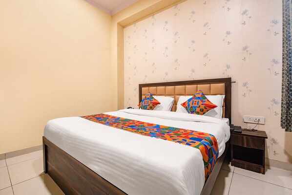 Uma cama bem arrumada com um cobertor e almofadas de padrão geométrico colorido, uma cabeceira de madeira e uma pequena mesa de cabeceira com um telefone e tomada.