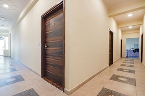 Um corredor com porta de madeira, soalho em azulejos e parede de cor clara.