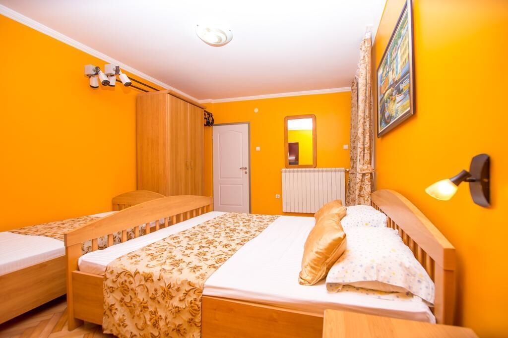 Quarto com duas camas de madeira, uma porta branca, radiador e um quadro na parede.