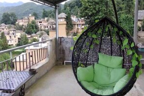 Uma cadeira suspensa com almofadas em uma varanda com vista para uma área residencial.