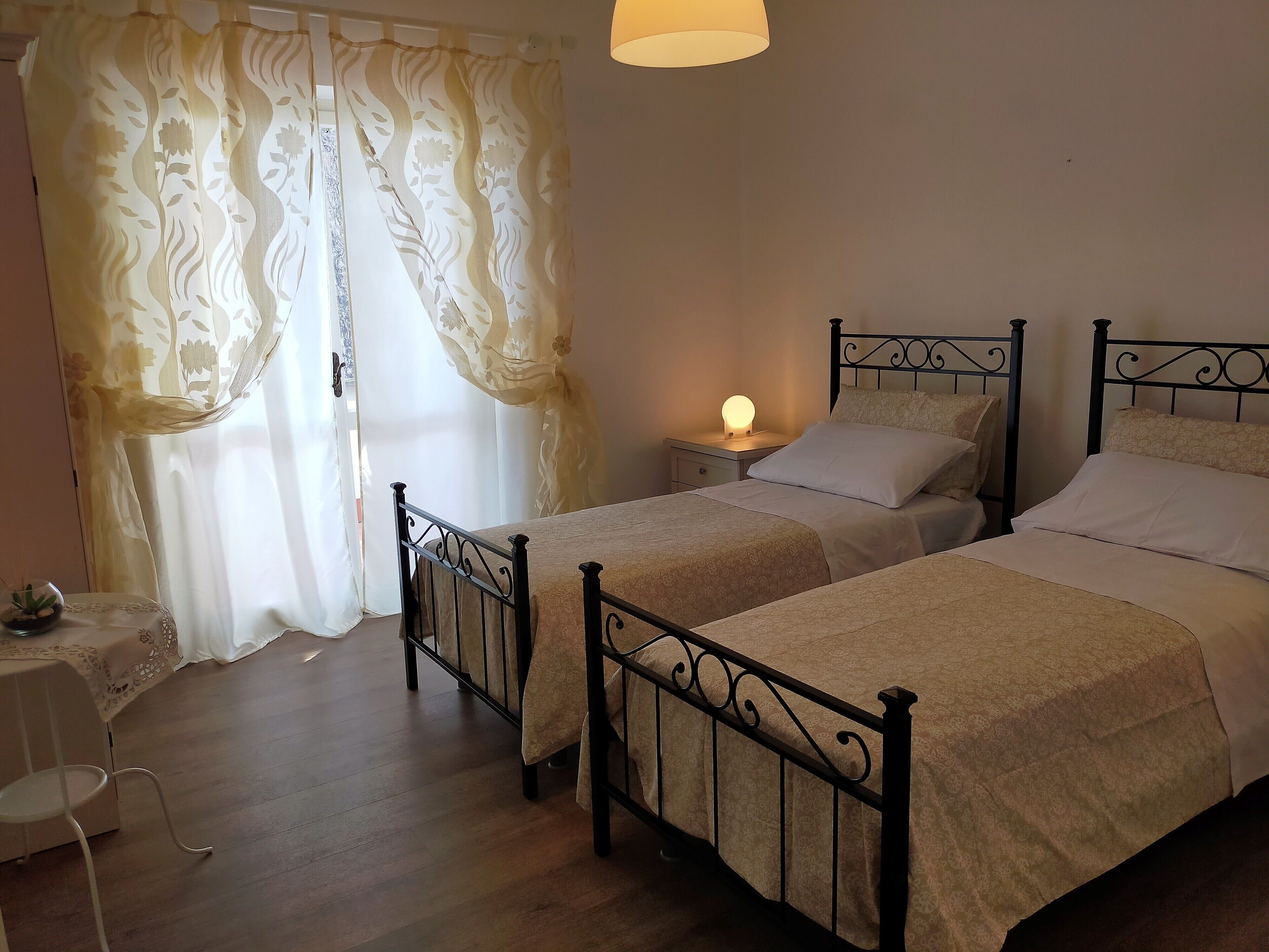 Quarto com duas camas, uma mesinha de cabeceira com abajur, uma cadeira e uma pequena mesa com planta.