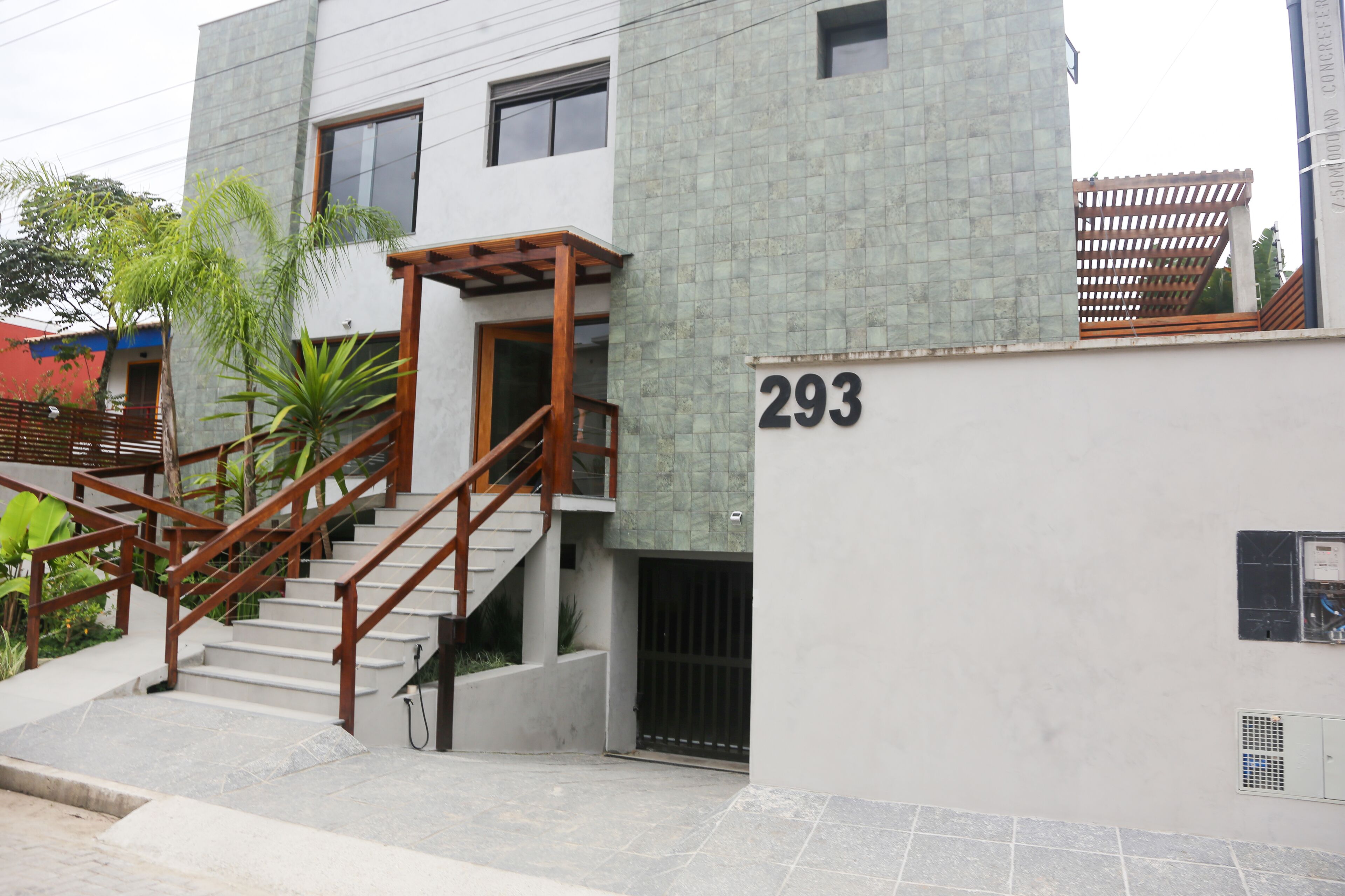 Um edifício moderno de dois andares com uma escadaria que leva à entrada, o número '293' na parede e um portão de acesso.