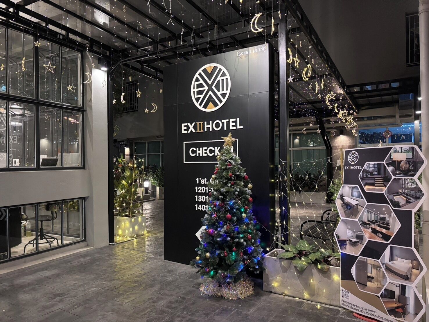 Exterior do EXIHOTEL com árvore de Natal, balcão de check-in e exposição de interiores de quartos.