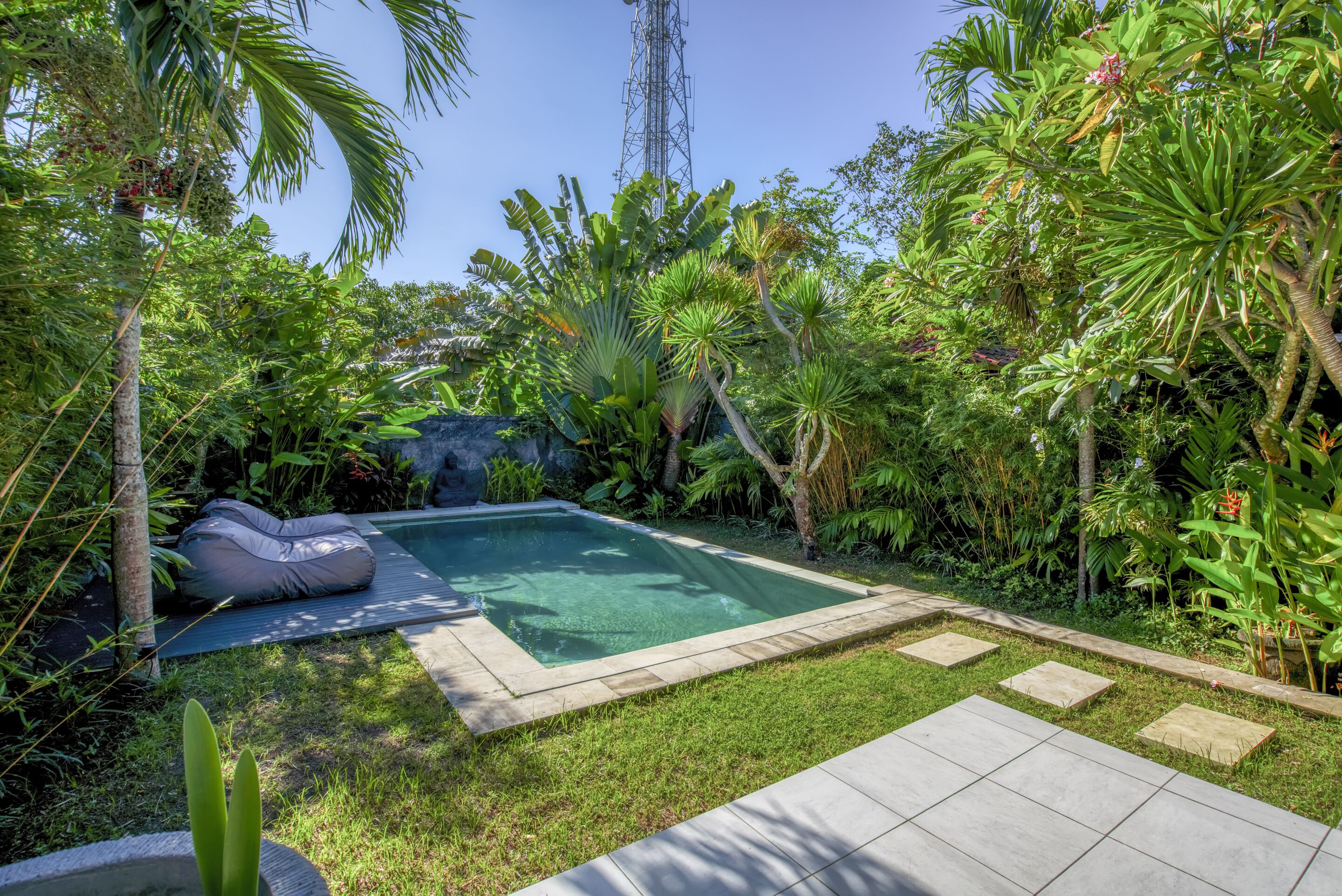 Uma piscina privativa rodeada por vegetação exuberante e um caminho de pedra que leva a um espaço de estar.