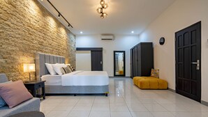 Quarto moderno com parede de destaque em pedra, uma cama grande, um sofá e um banquinho amarelo.