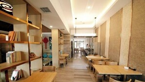 Um restaurante moderno com mesas e cadeiras de madeira, um balcão comprido e estantes de livros.