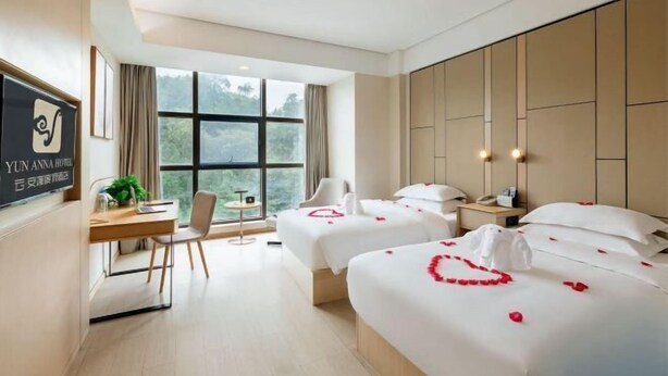 Quarto de hotel com duas camas, uma escrivaninha, uma cadeira, uma televisão e uma janela grande.