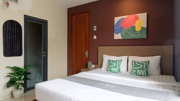 Quarto de hotel com cama, planta em vaso, porta e uma obra de arte na parede.