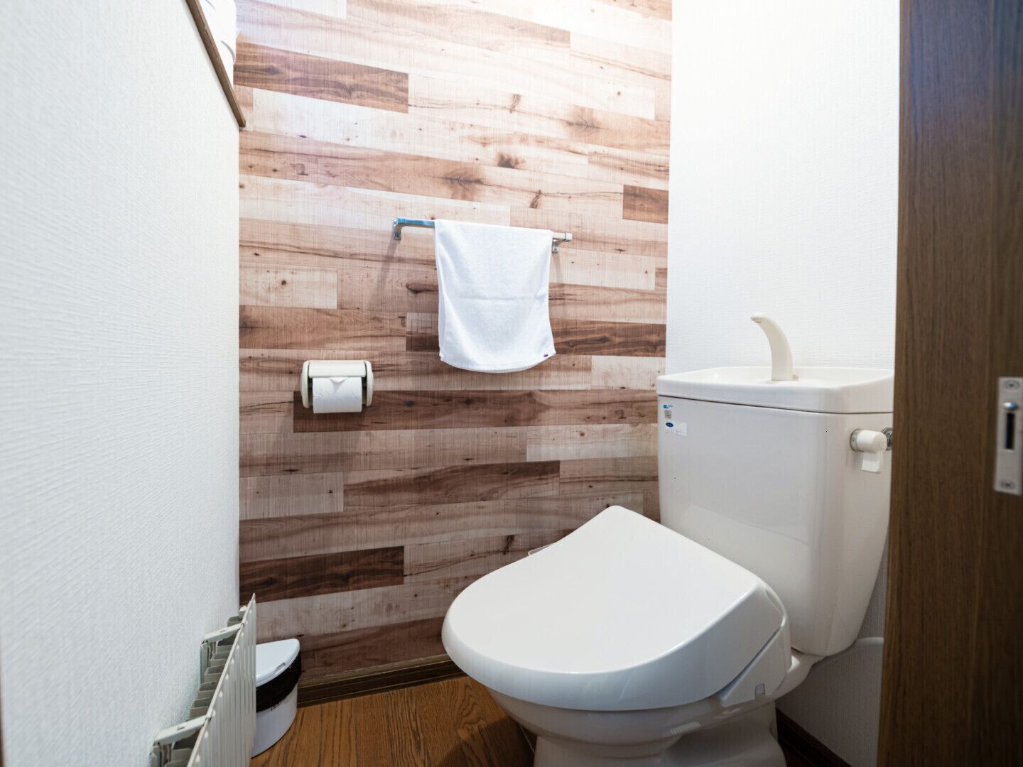 Um banheiro pequeno com parede de madeira, vaso sanitário, toalha pendurada em um porta-toalhas e dispensador de papel higiênico.