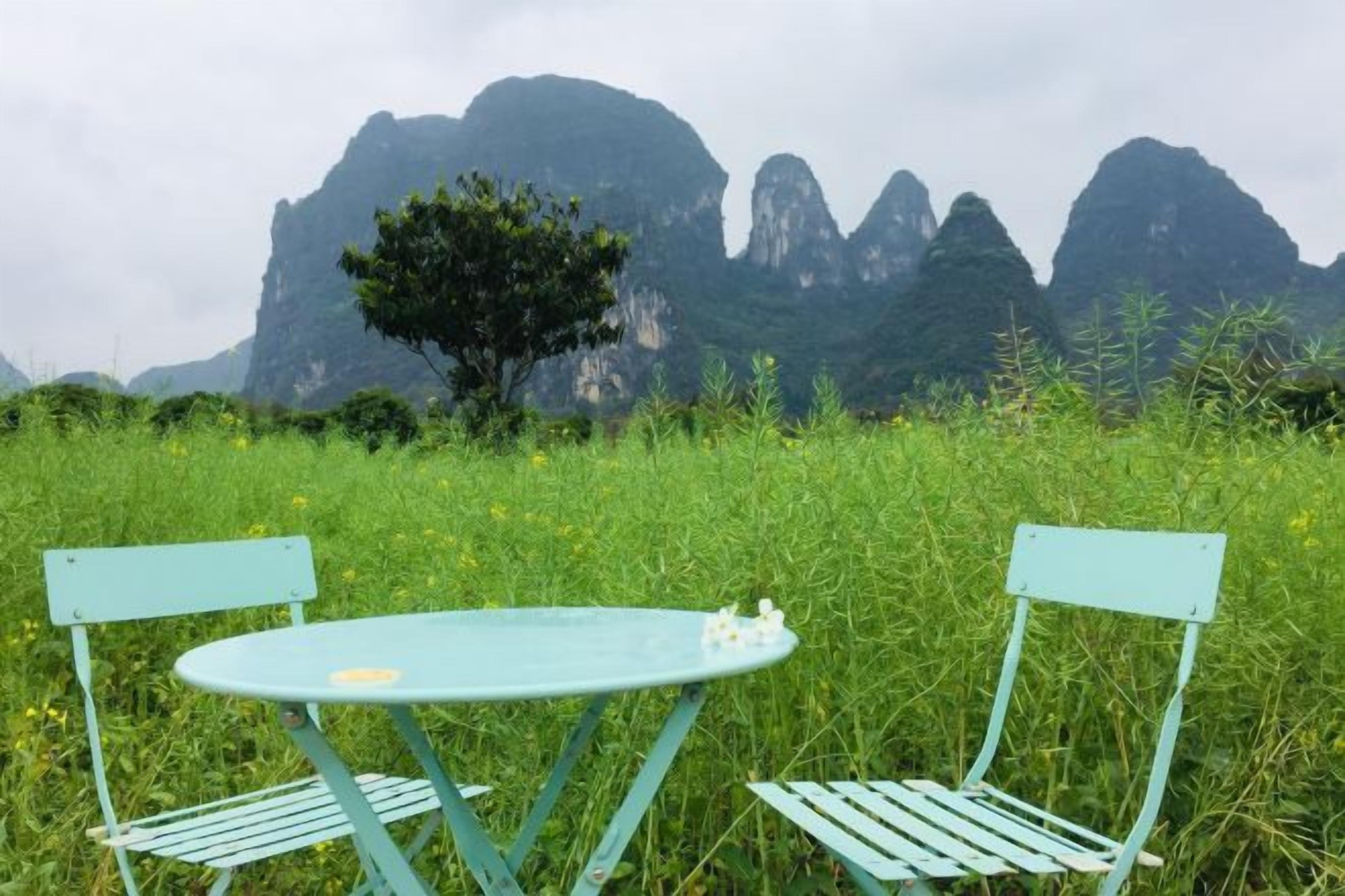 Uma mesa e duas cadeiras em um campo gramado, com montanhas ao fundo.