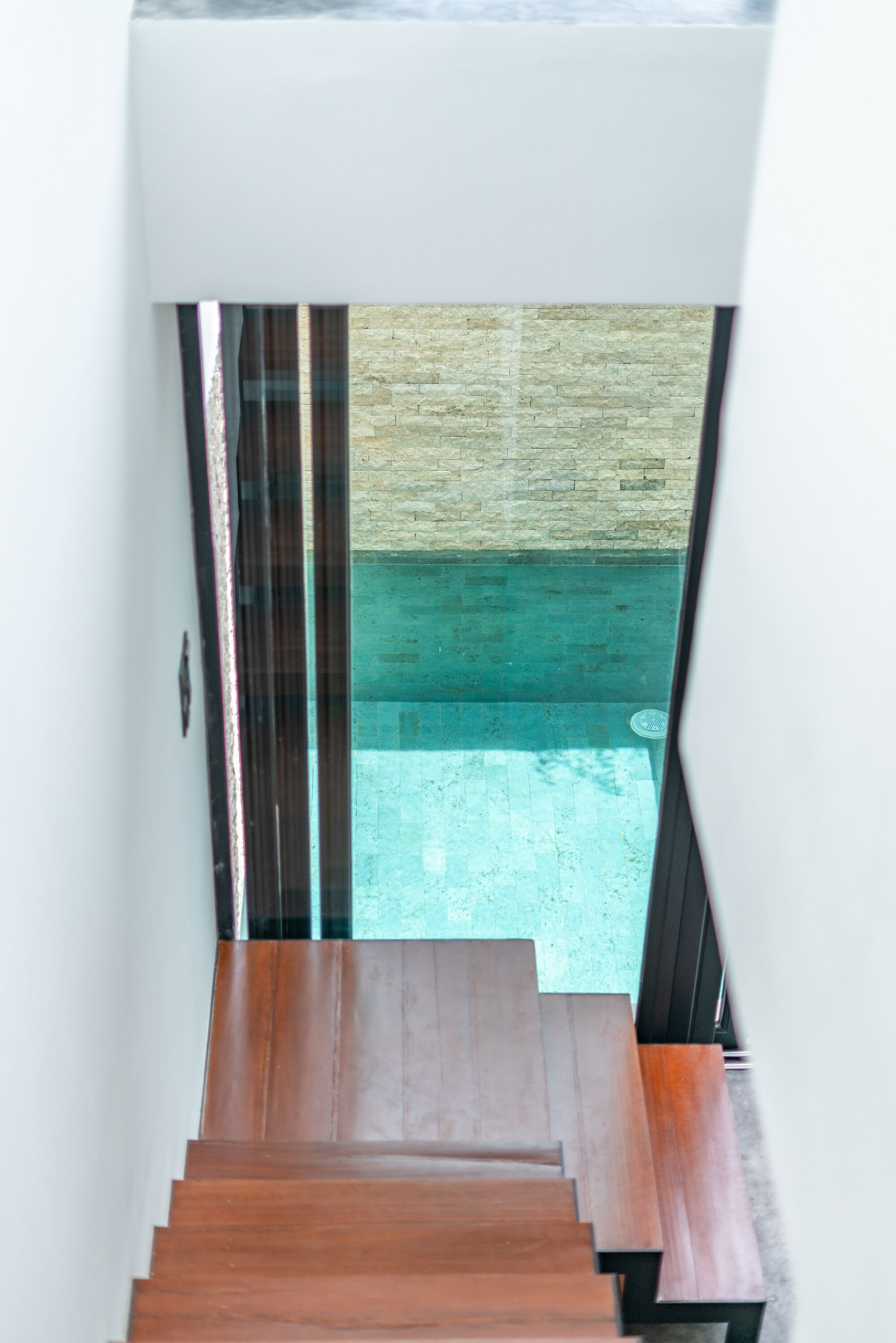 Escadaria que leva a uma área de piscina com muro de pedra e porta de vidro.