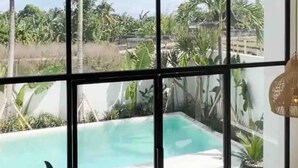 Quarto com grandes janelas com vista para uma piscina e vegetação exuberante.