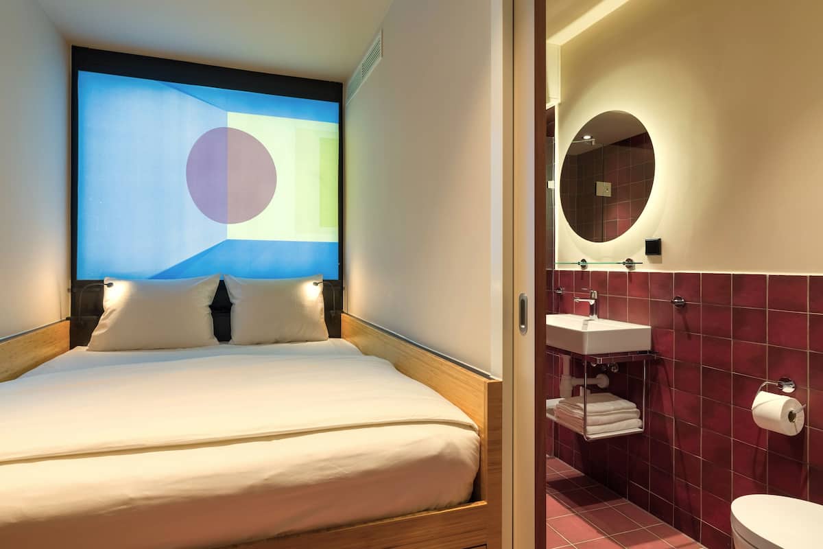 Quarto de hotel com cama, televisão presa na parede, banheiro com pia, espelho e vaso sanitário.