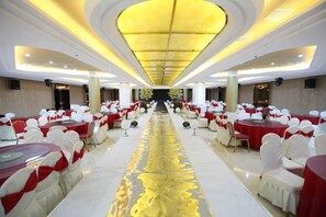 Uma sala de banquetes com mesas redondas e cadeiras, um corredor central e piso espelhado.