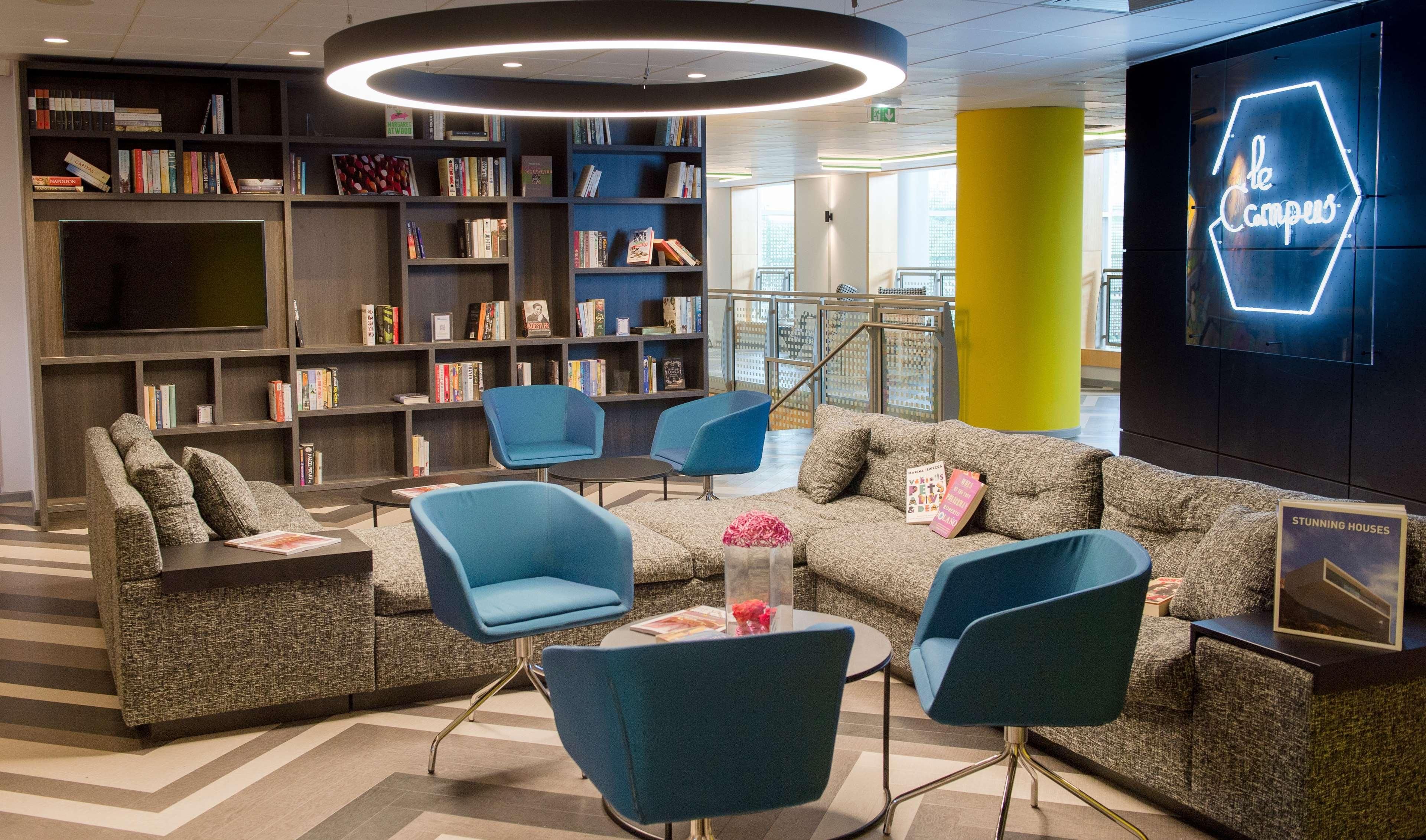 Um espaço de leitura moderno com sofás, cadeiras e uma grande estante de livros.