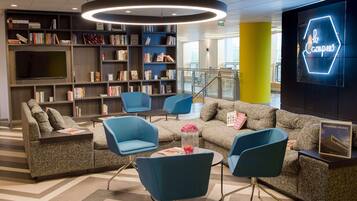 Um espaço de leitura moderno com sofás, cadeiras e uma grande estante de livros.