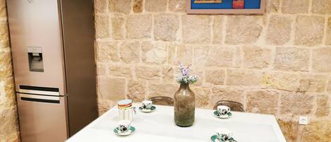 Uma cozinha com parede de pedra, geladeira, mesa com um vaso de flores e um quadro na parede.
