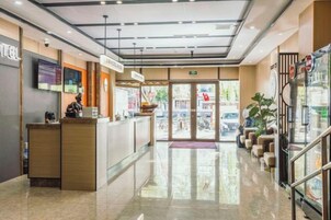 Um hall de hotel com uma receção, um ecrã digital e uma escadaria para o andar superior.