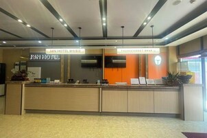 Uma área de recepção de hotel com balcão, tela digital e placa com o nome do hotel.