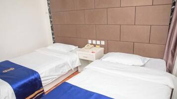 Quarto de hotel com duas camas de solteiro, uma mesinha de cabeceira com telefone e luminária fixada na parede.