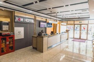 Uma área de recepção de hotel, com balcão de atendimento, televisão e tela digital exibindo informações.