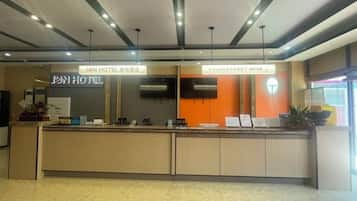 Uma área de recepção de hotel com balcão, televisão e placa com o nome do hotel.